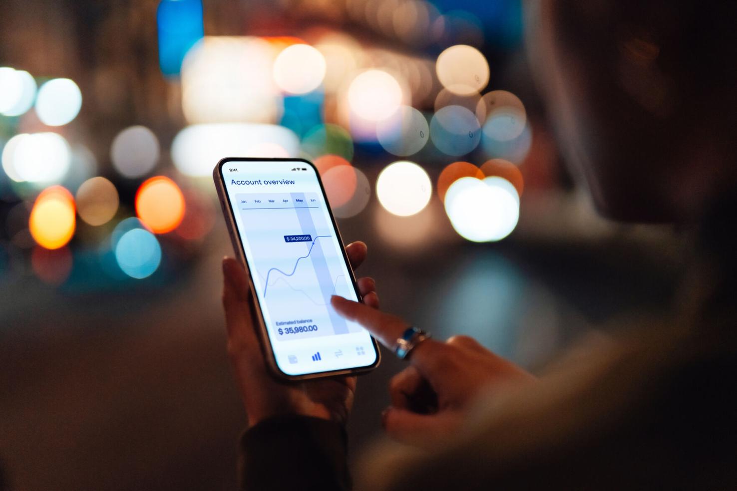 Over the shoulder view of young woman managing finance via trading app ...