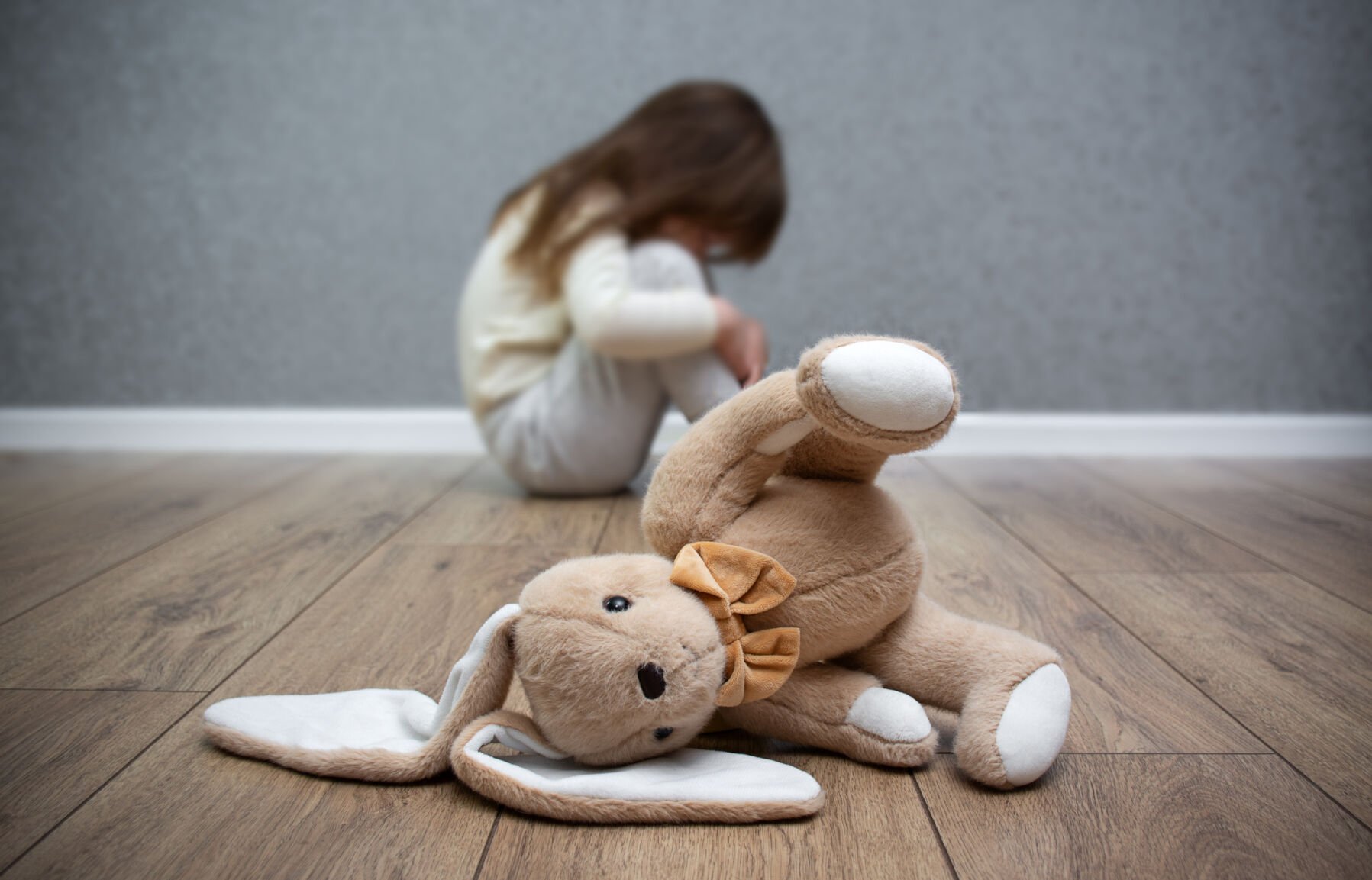 A stuffed bunny on the floor, a scared child sitting behind it. Child ...