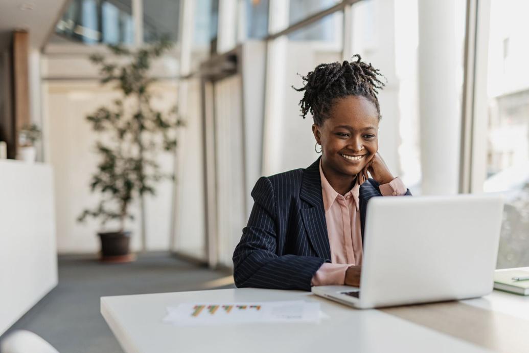 A smiling businesswoman works at her laptop, illustrating a joyful and ...