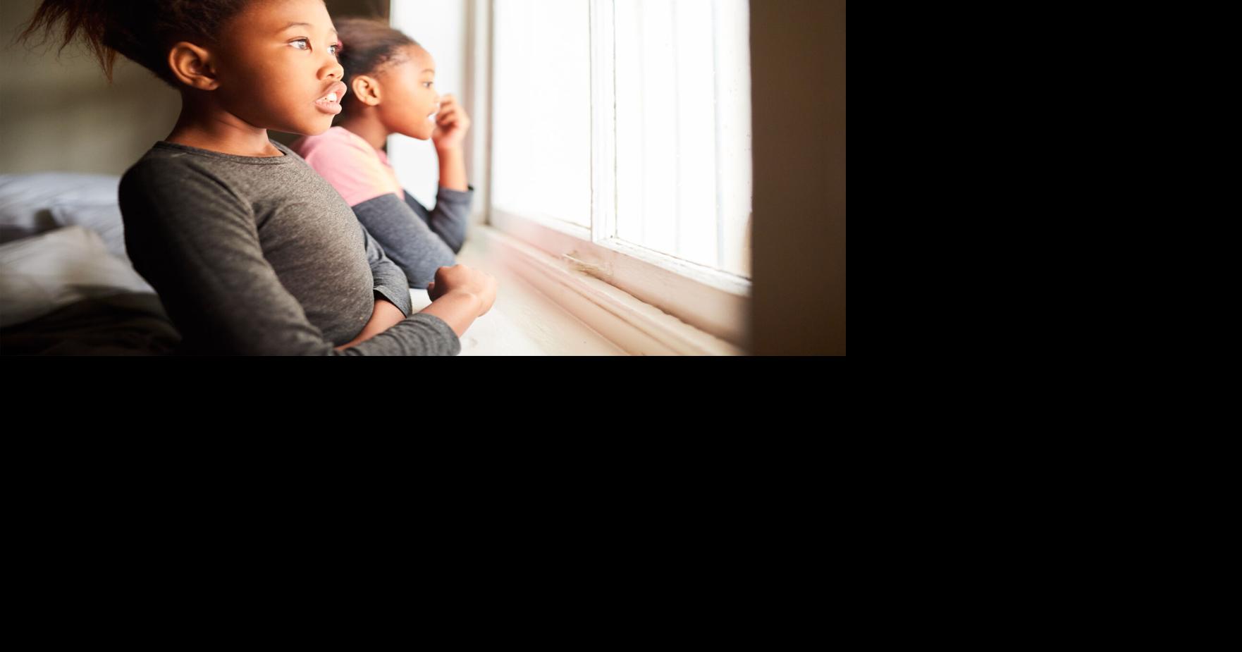 Two little sisters looking through a window at home