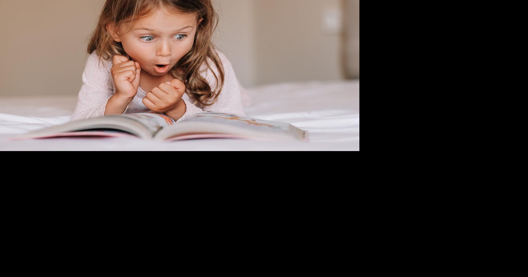 Fantasy literature. Emotional child girl read interesting book in bed ...