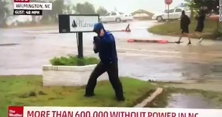 Men stroll past weatherman in hurricane