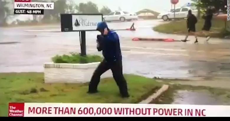 Men stroll past weatherman in hurricane